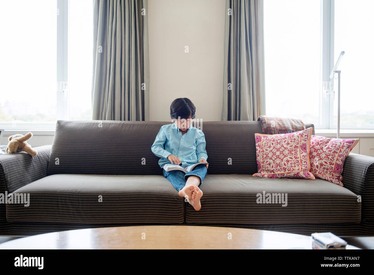 Boy reading book while sitting on sofa at home Stock Photo - Alamy