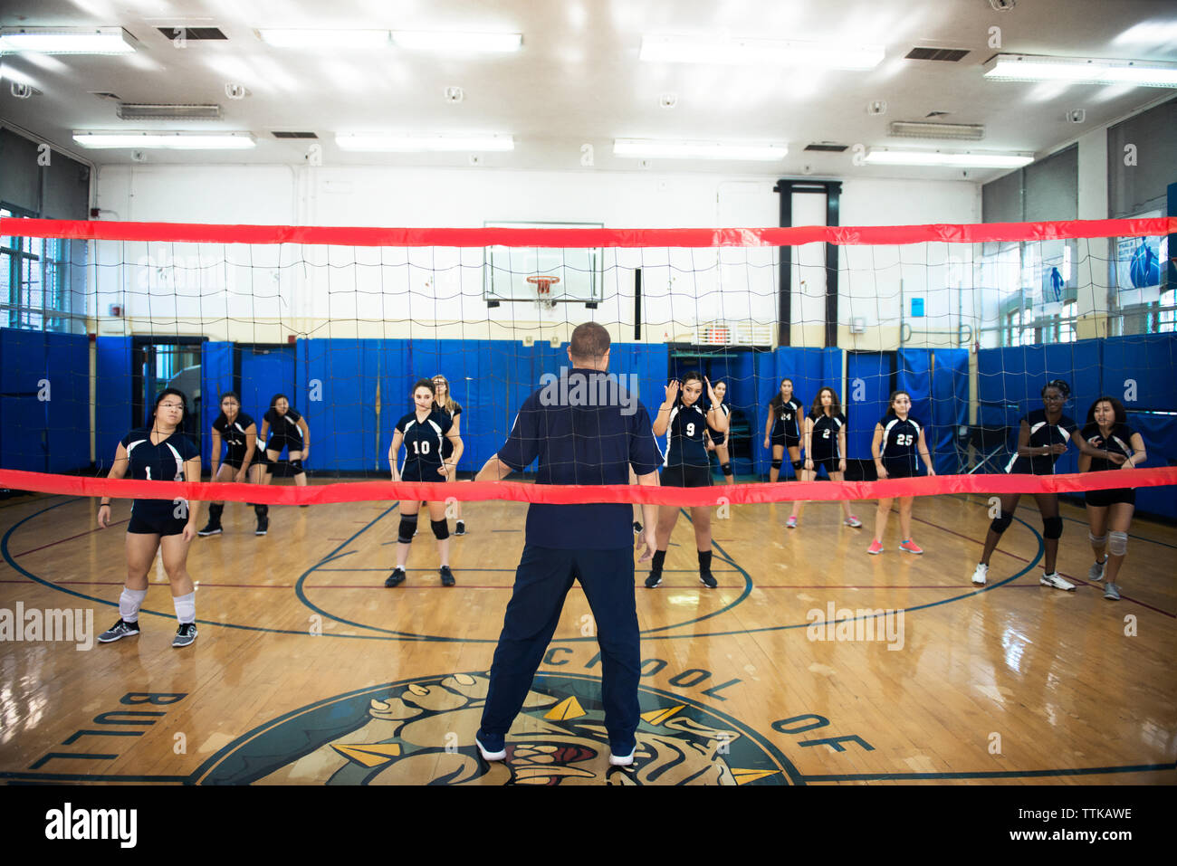 Male coach teaching exercise to female volleyball team Stock Photo - Alamy