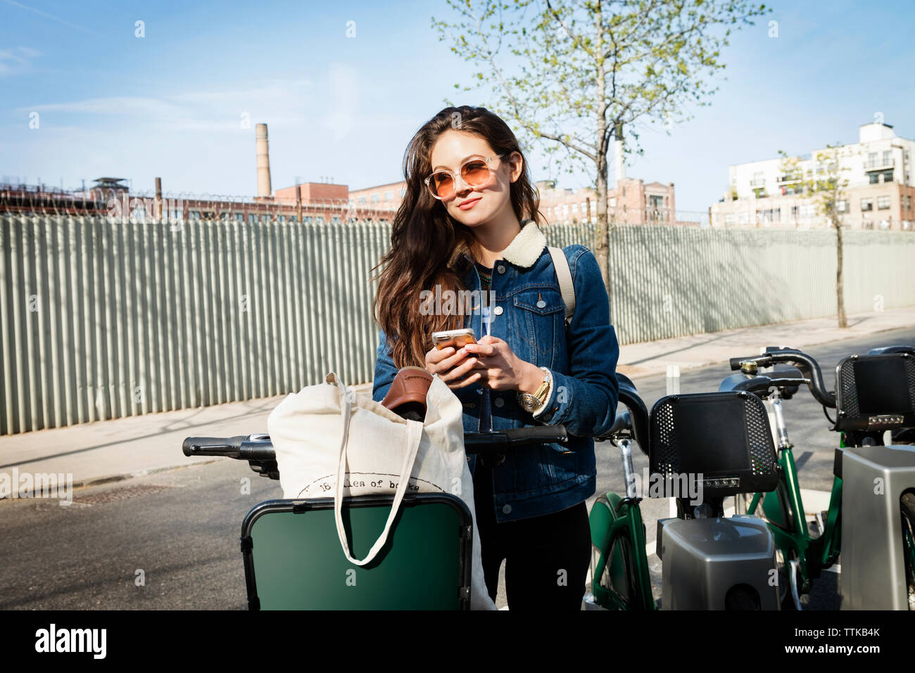 Woman using phone while standing by bicycle on city street Stock Photo ...