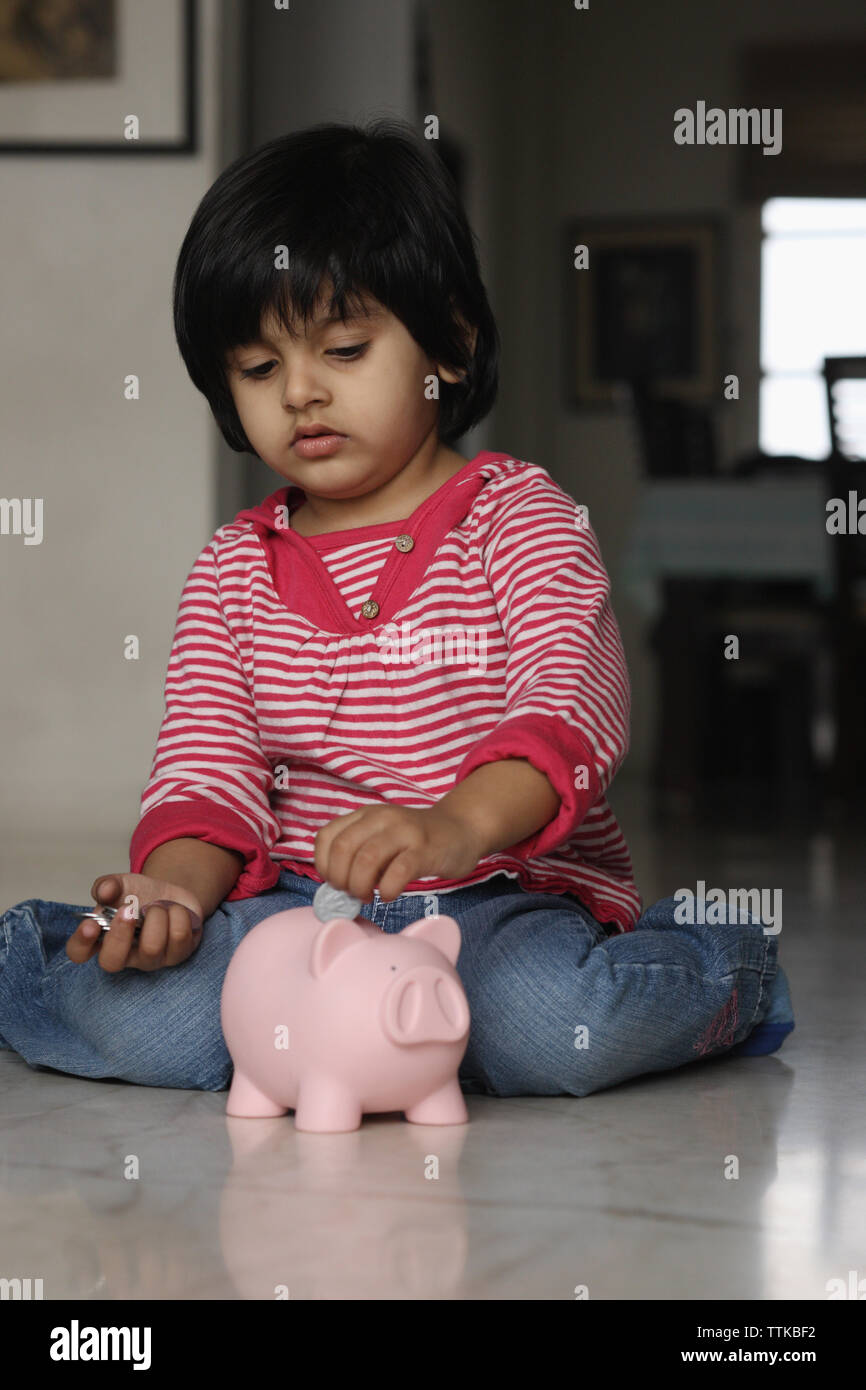 Indian girl putting a coin into a piggy bank Stock Photo - Alamy
