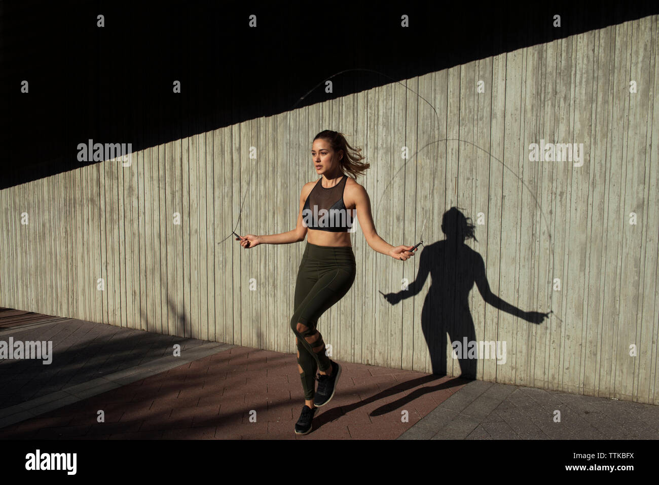 Young woman skipping while exercising against wall Stock Photo - Alamy