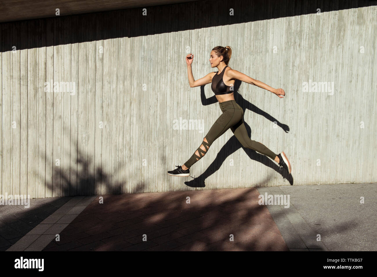 Young woman jumping while exercising against wall Stock Photo - Alamy