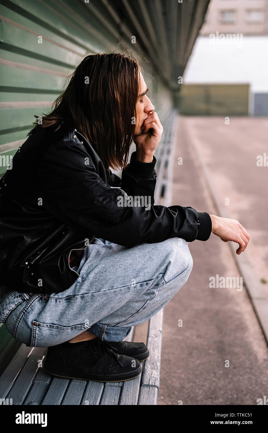 Side view of man with eyes closed crouching on bench by wall Stock ...