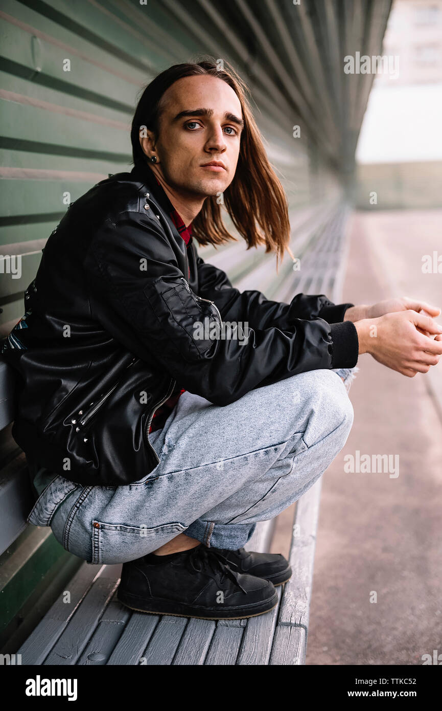 Portrait of man crouching on bench by wall Stock Photo - Alamy