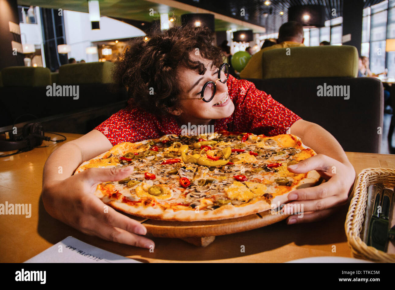 Happy woman holding pizza on wooden table while sitting in restaurant ...