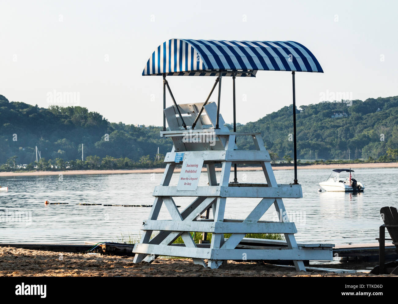 A white lifeguard stand with a blue and white striped cover at a beach ...