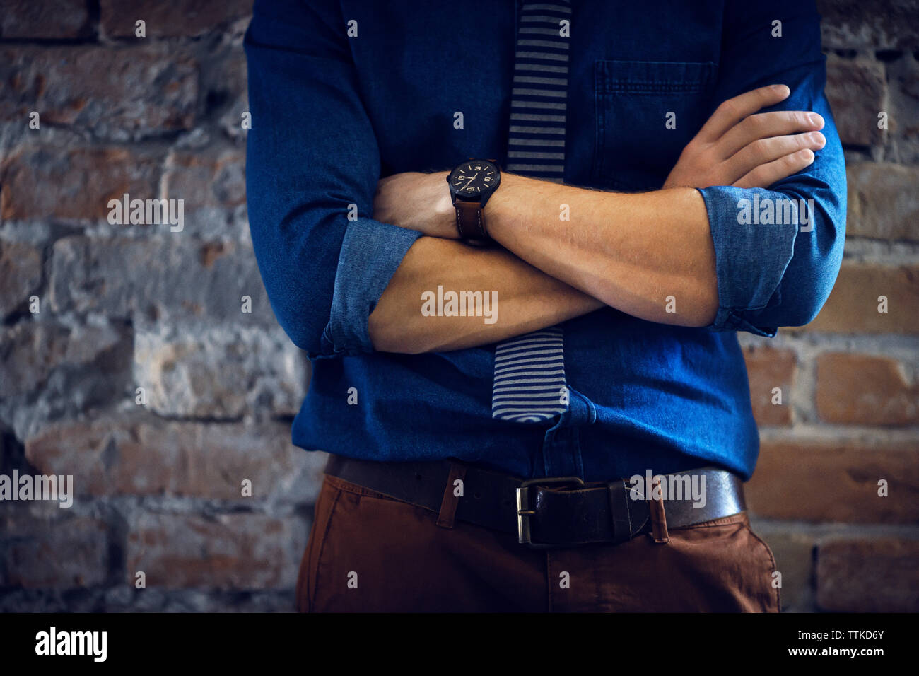 Midsection of businessman with arms crossed standing against brick wall ...