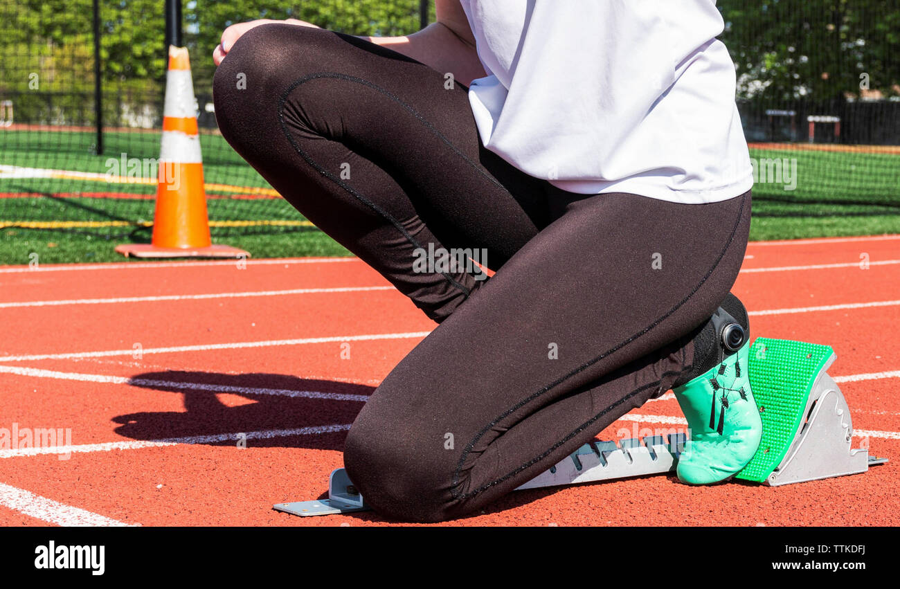 A high school sprinter is getting set into the starting blocks to ...