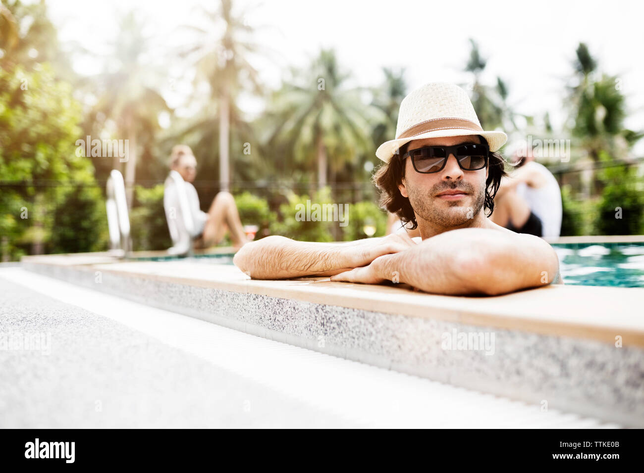 Thoughtful man relaxing in swimming pool with friends in background ...