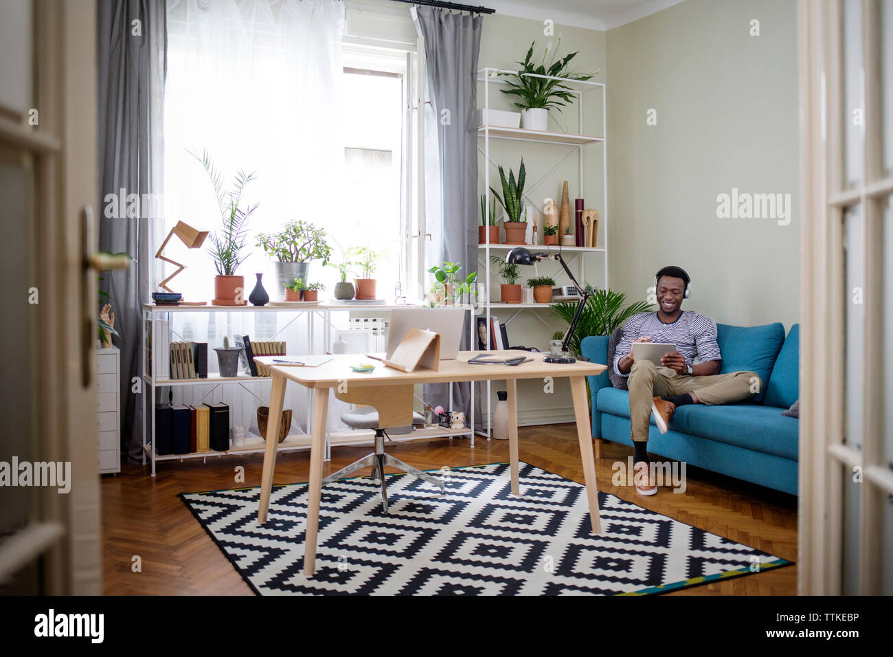 Happy young man using tablet computer while sitting on sofa at home ...
