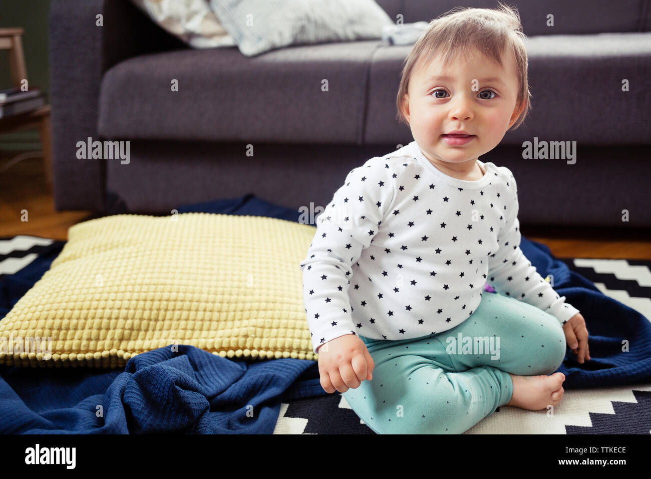Portrait of cute baby girl sitting on rug in living room Stock Photo ...