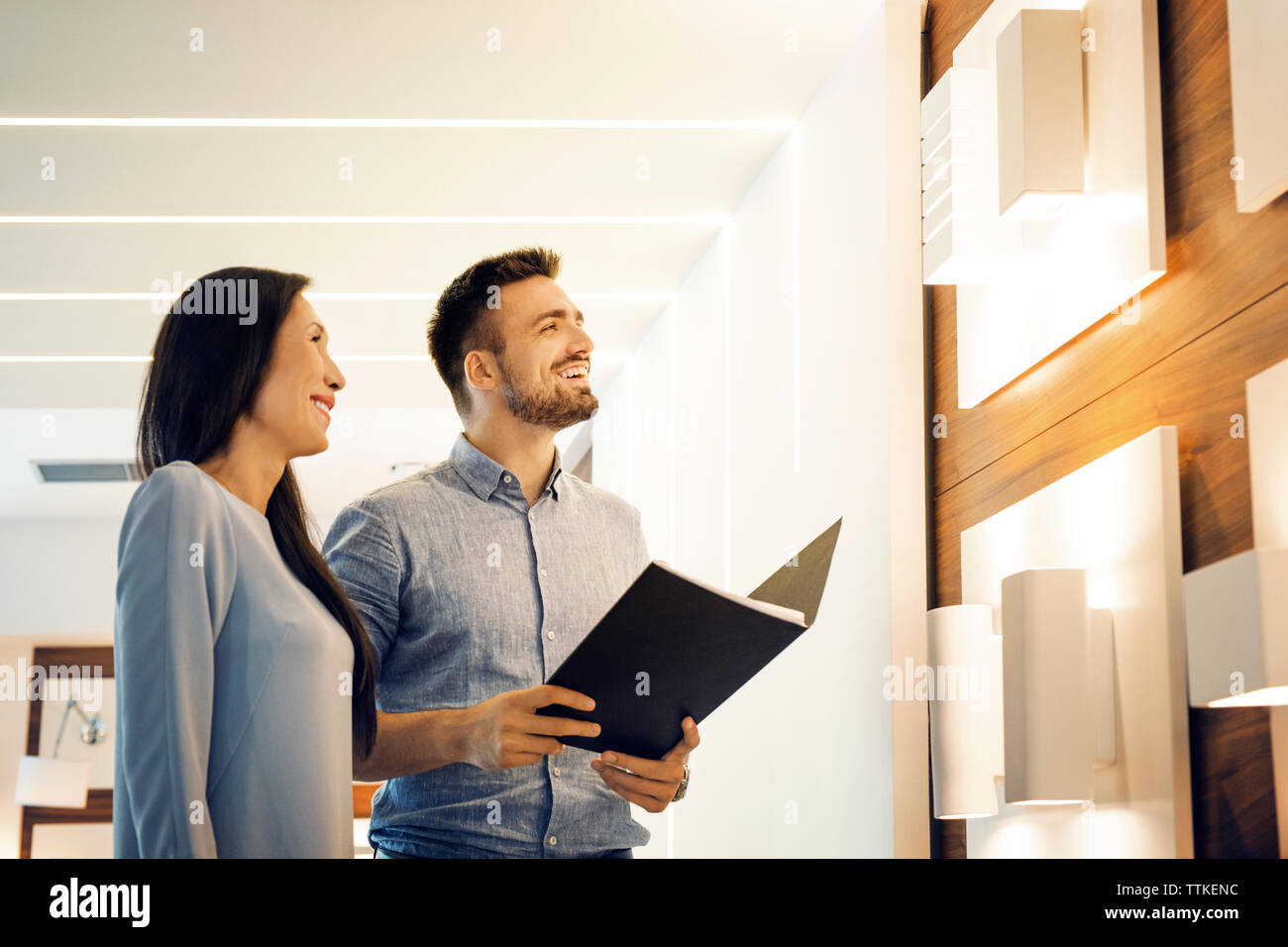 Happy business people looking at illuminated lamps on wall in office ...