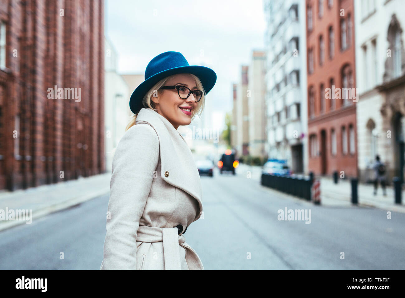 Side view of happy woman looking away while standing on city street ...