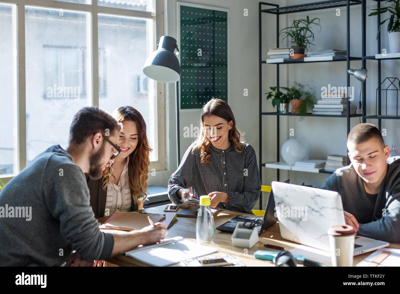 Happy friends studying at table by window in classroom Stock Photo - Alamy