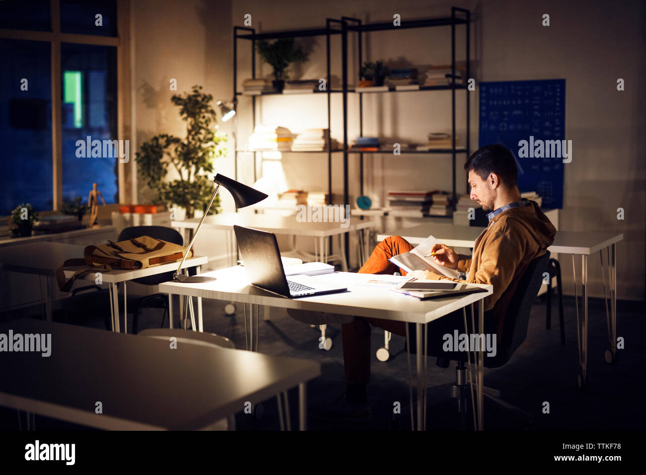 Man studying while sitting by table in library Stock Photo - Alamy