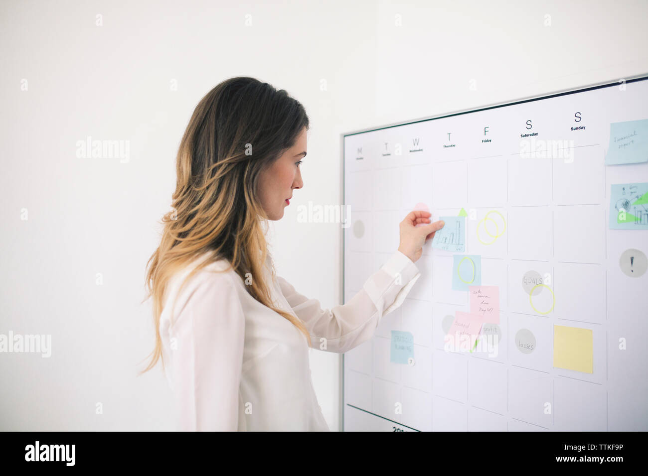 Side view of businesswoman sticking adhesive notes on whiteboard in ...