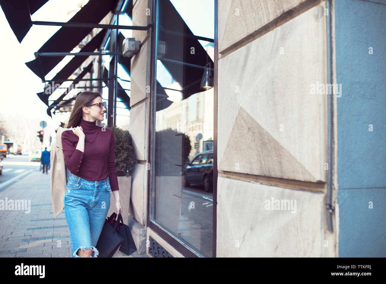 Woman looking in shop window while walking on sidewalk Stock Photo - Alamy