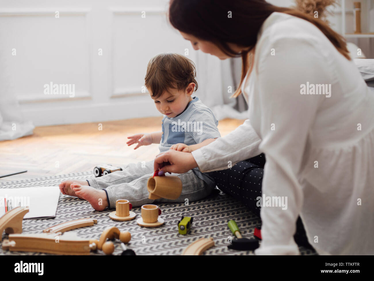Baby boy looking at mother pouring tea in toy teacup at home Stock ...