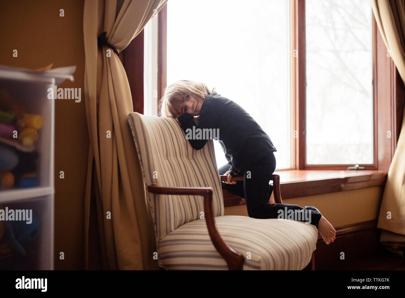 Side view portrait of girl kneeling on armchair by window at home Stock ...