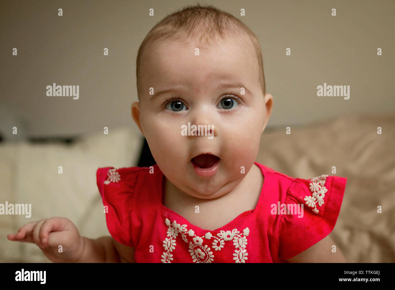 Close-up portrait of cute surprise baby girl with mouth open at home ...