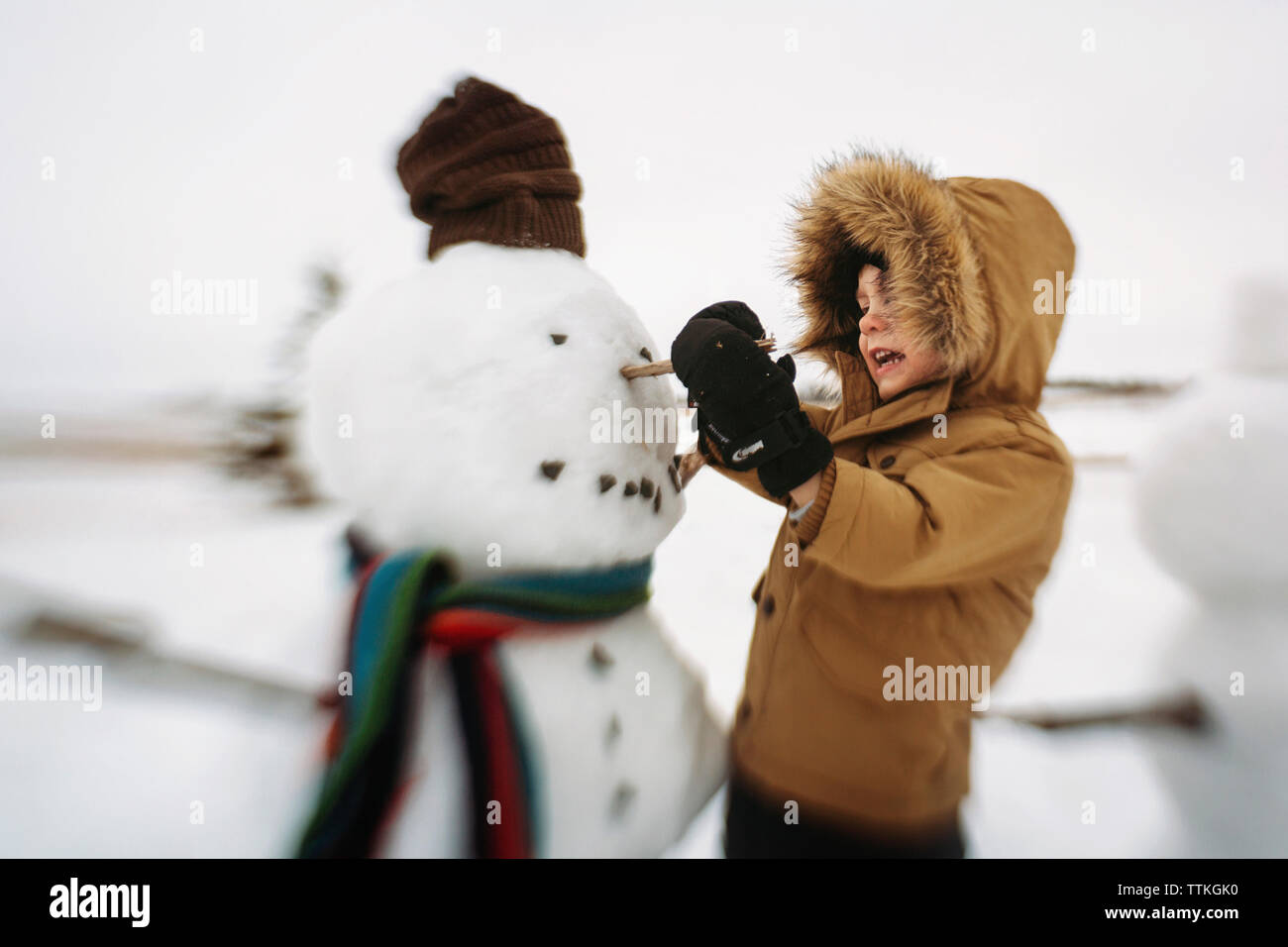 Boy making snowman while standing on field Stock Photo - Alamy