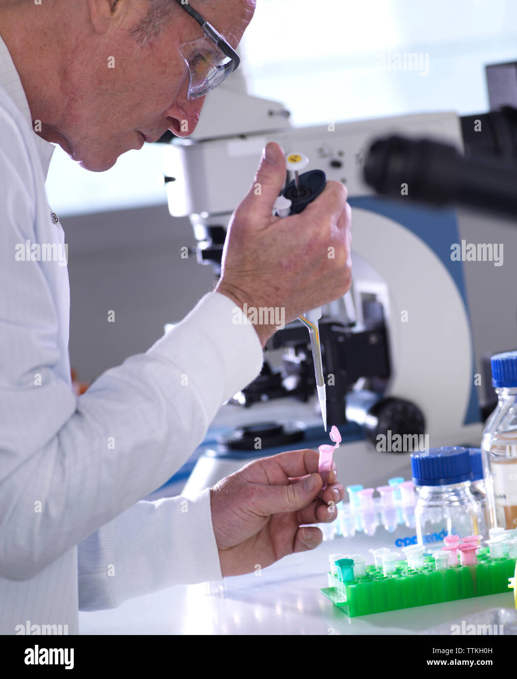 Side view of male scientist pipetting samples in vial on table at ...