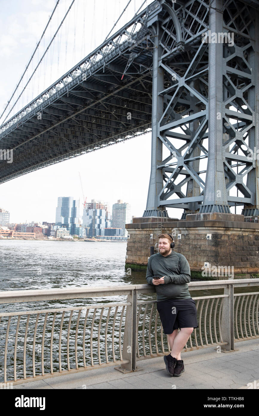 Full length of overweight man listening music while standing by river ...