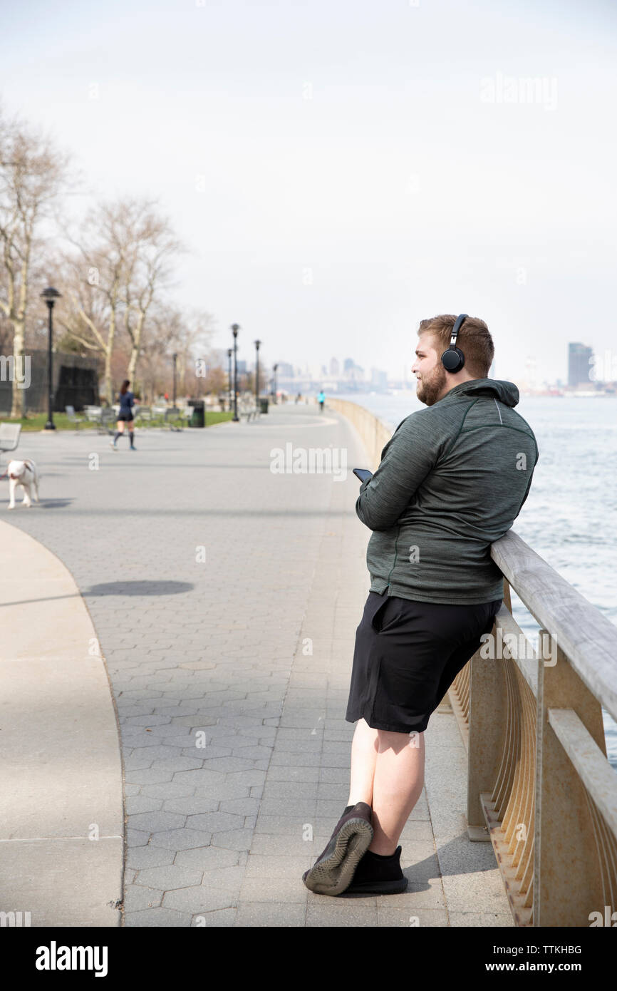 Full length of overweight man listening music on headphones while ...