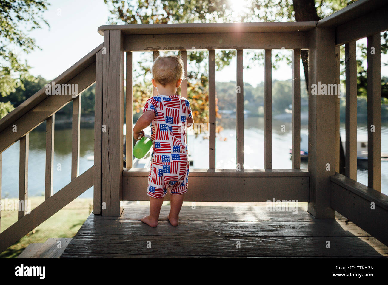 Rear view of baby boy standing by wooden railing against lake Stock ...