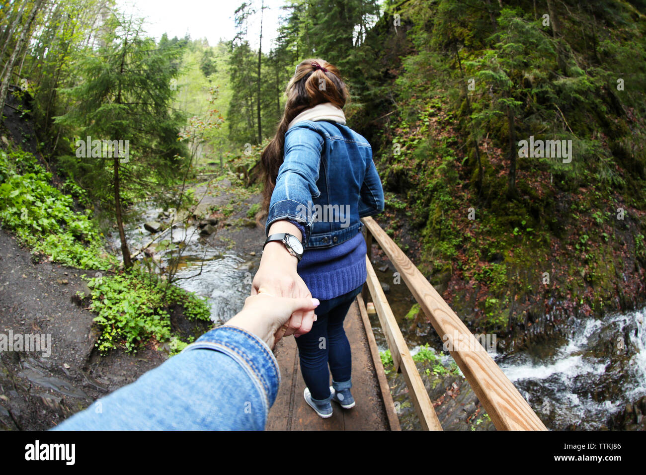 People walking across wooden bridge through mountain river. Follow me ...