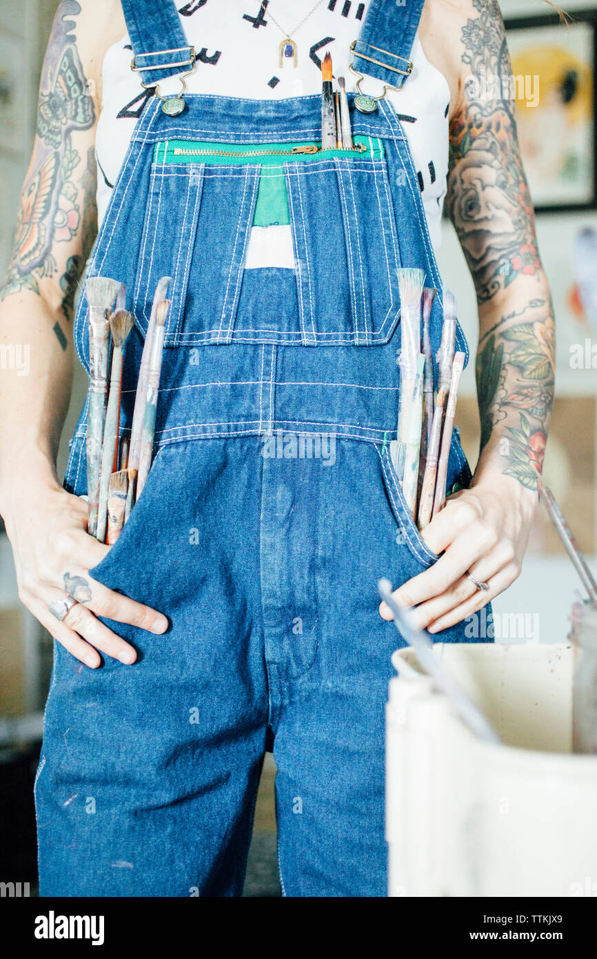 Midsection of female artist with hands in pockets standing in studio ...