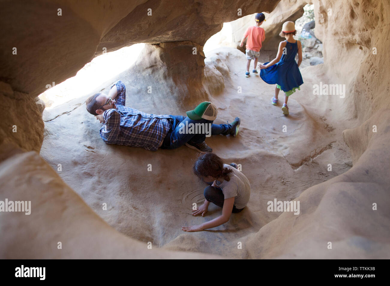 Father relaxing while children playing in cave Stock Photo - Alamy