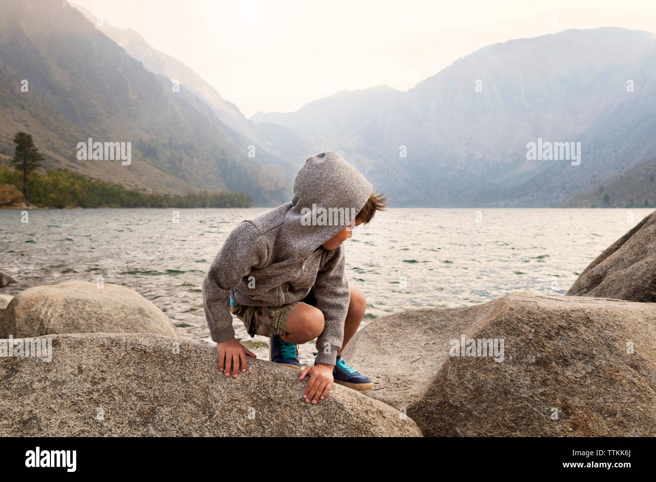 Boy crouching on rocks against Convict Lake and mountains Stock Photo ...