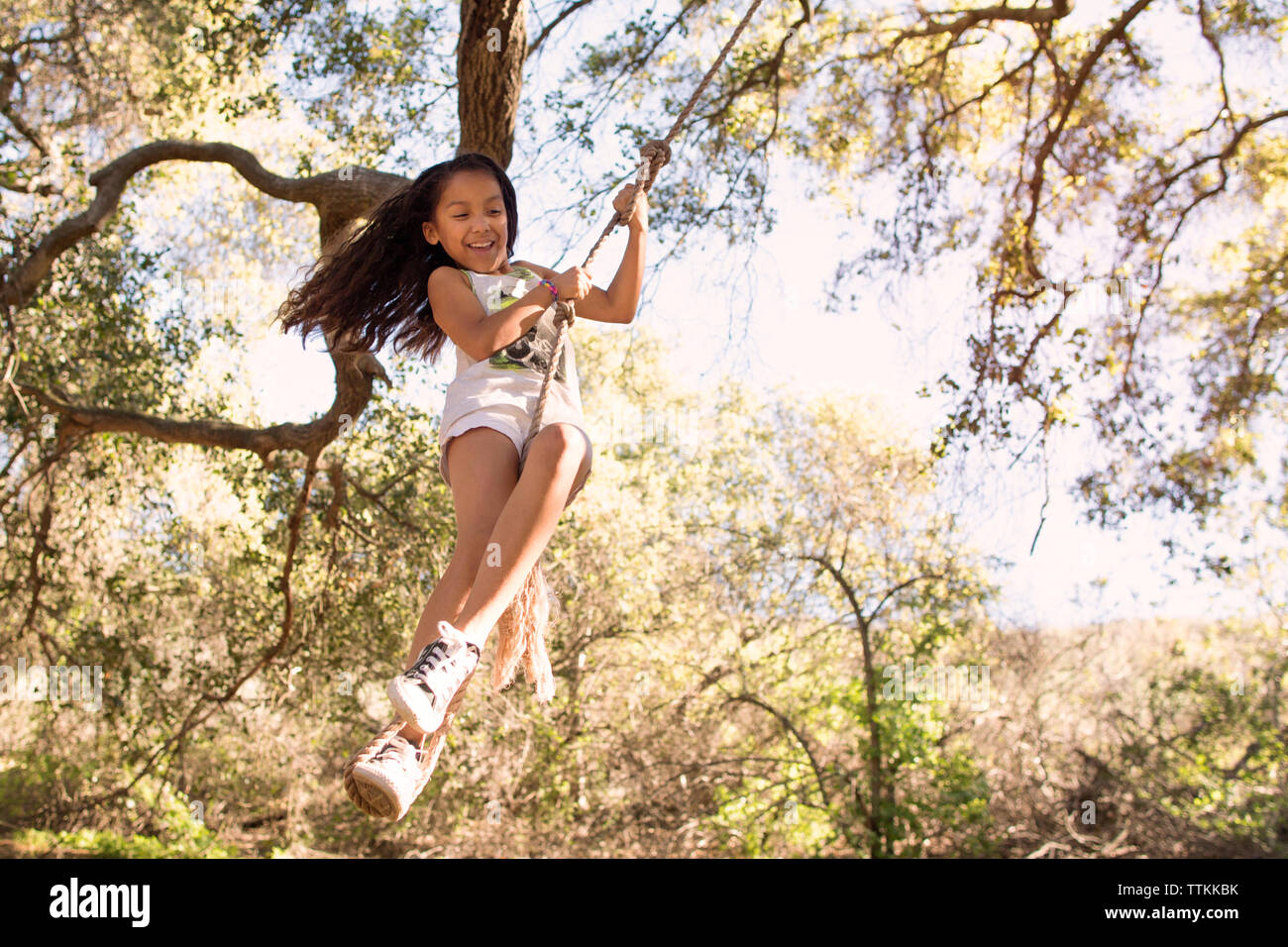 Cheerful girl playing on rope swing in forest Stock Photo - Alamy