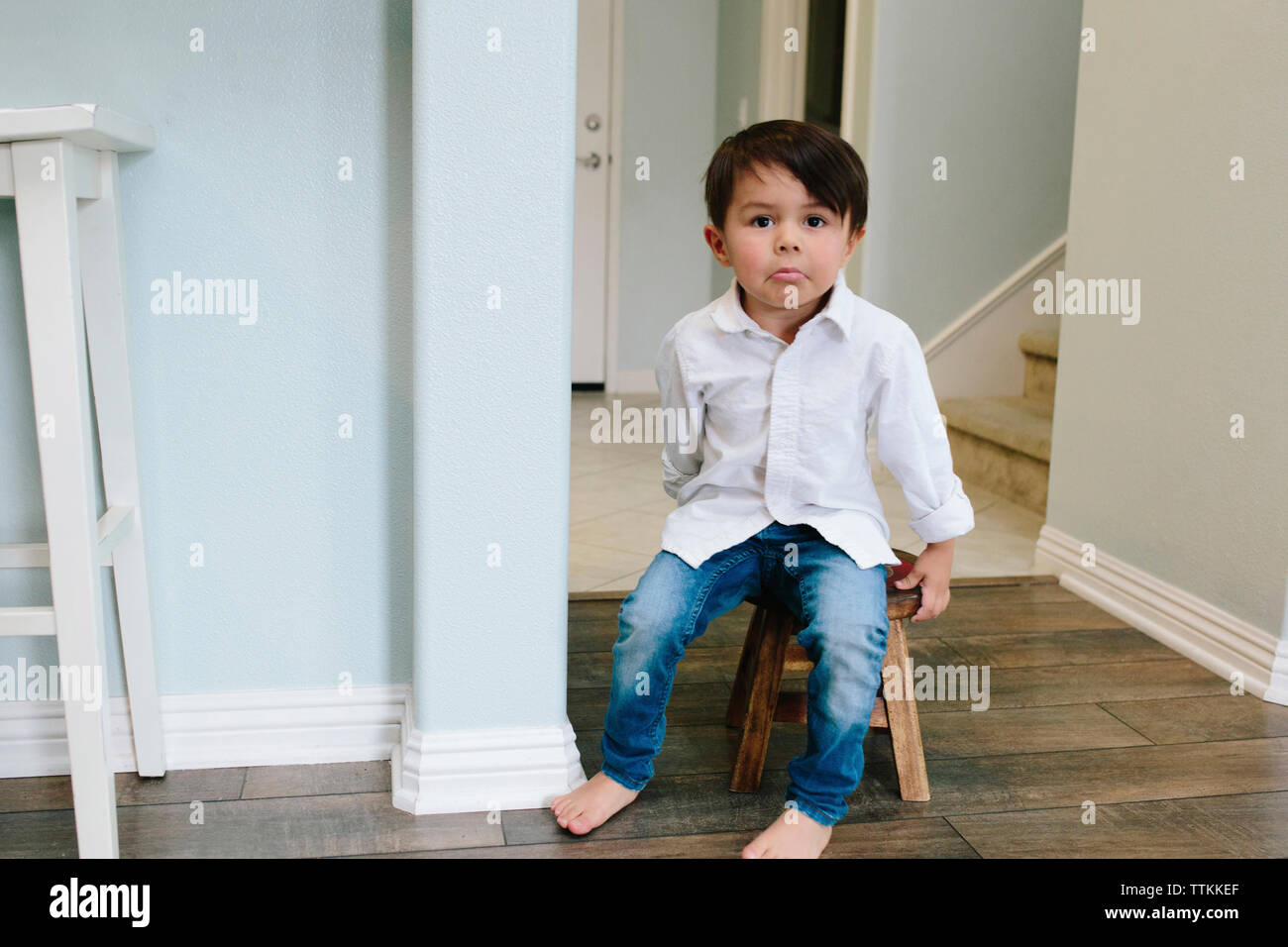 Portrait of cute boy sitting on stool at home Stock Photo - Alamy