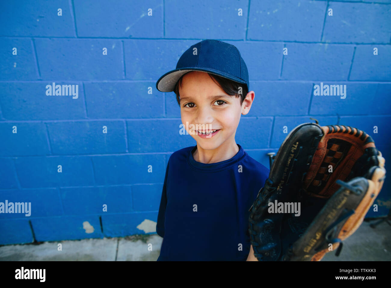 Portrait of happy boy wearing baseball glove standing against wall ...