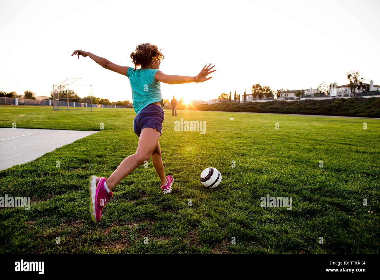 Full length of girl playing football on grassy field during sunset ...