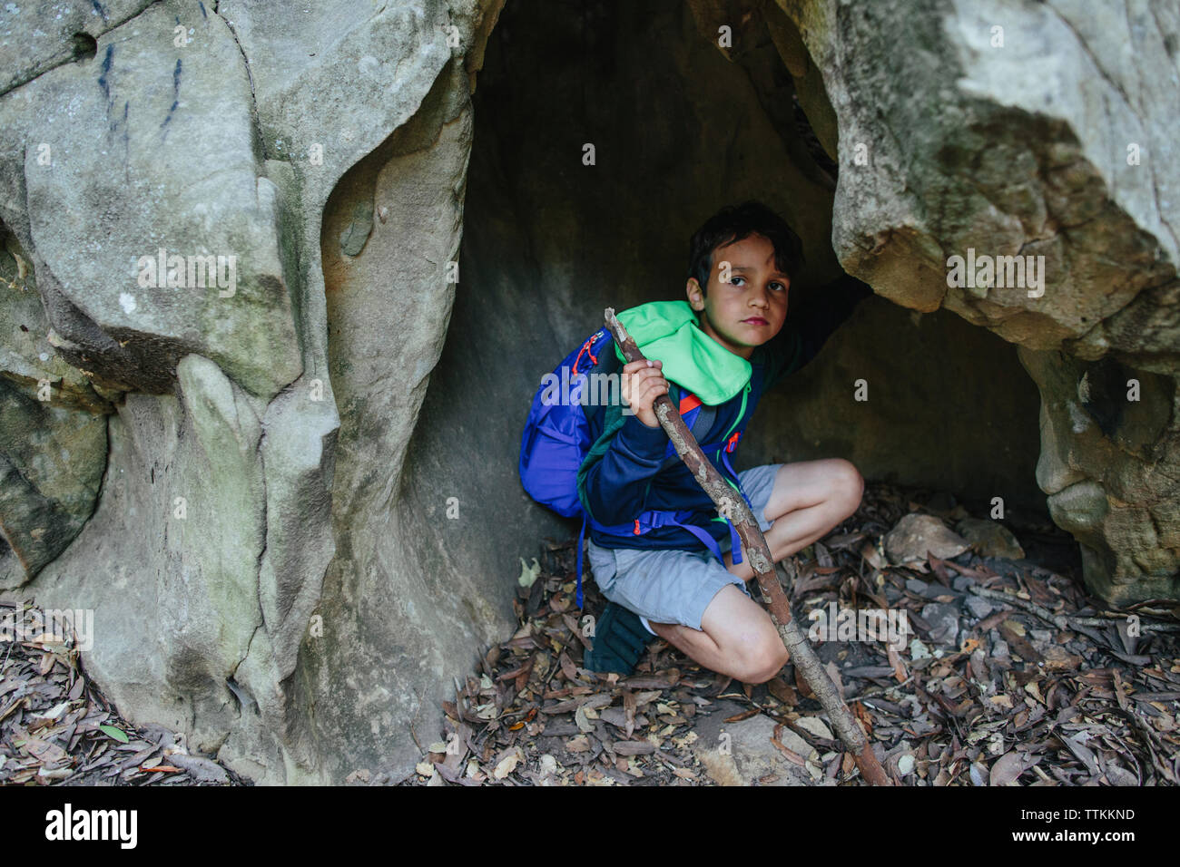Boy with backpack looking away while crouching in rock formation Stock ...