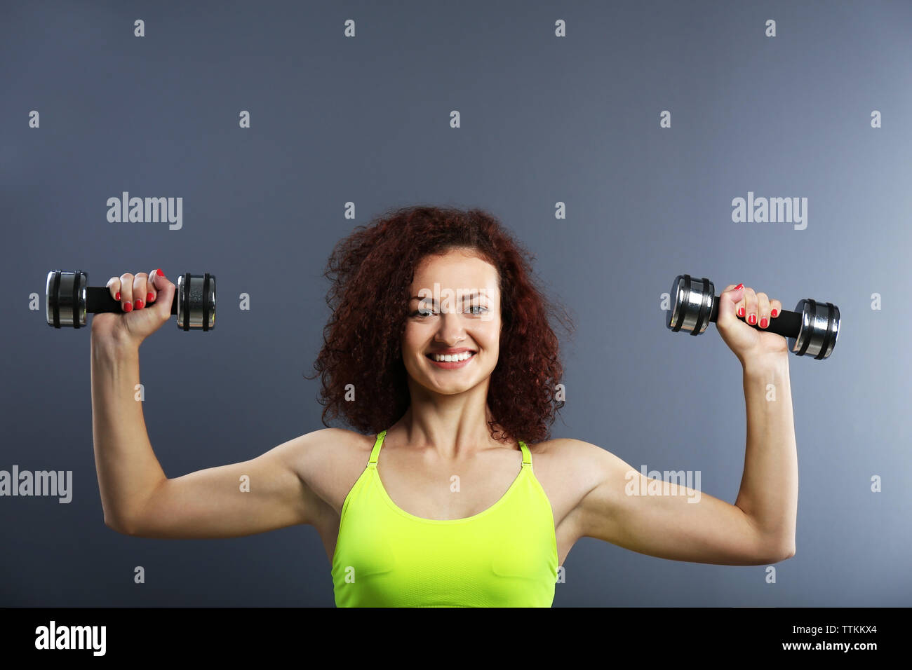 Attractive woman exercising with dumb bells on grey background Stock ...