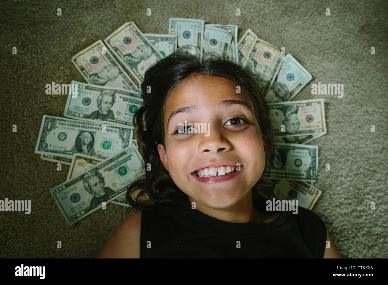 Overhead portrait of cheerful girl with paper currency around her head ...