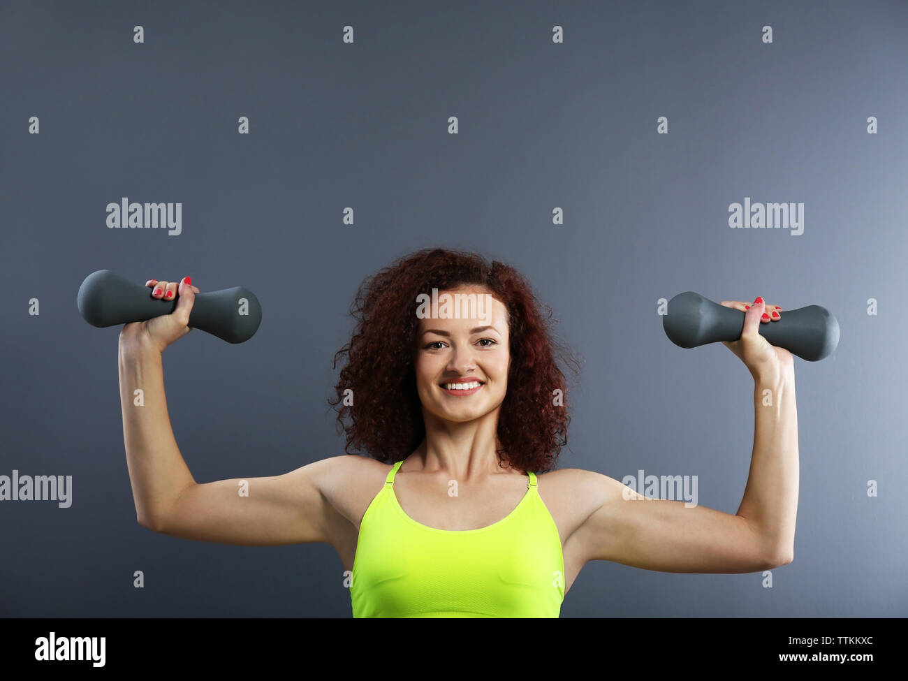 Attractive woman exercising with dumb bells on grey background Stock ...