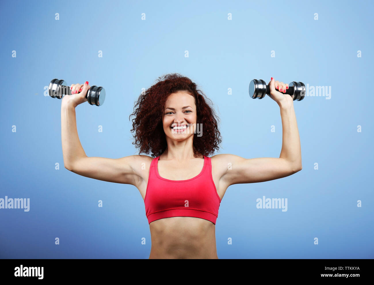 Attractive woman exercising with dumb bells on blue background Stock ...
