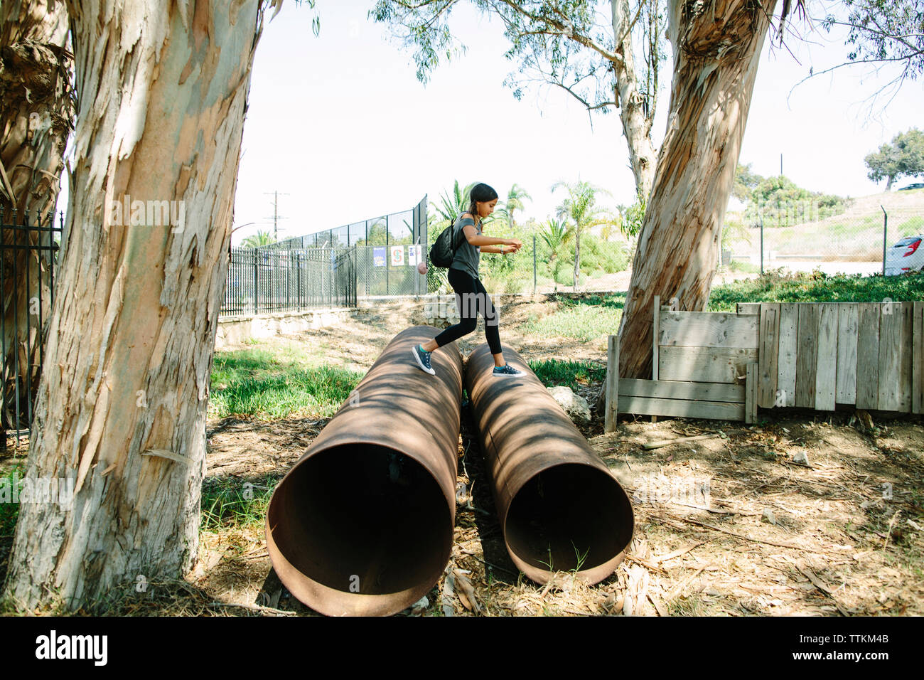Side view of girl with backpack jumping on pipes against clear sky ...