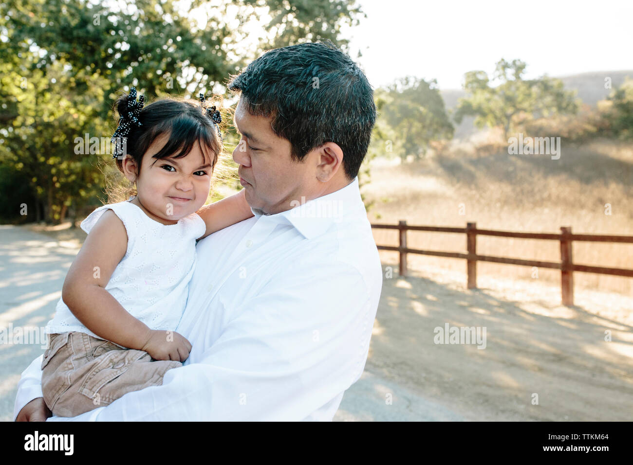 Side view of father looking at cute daughter making face while standing ...