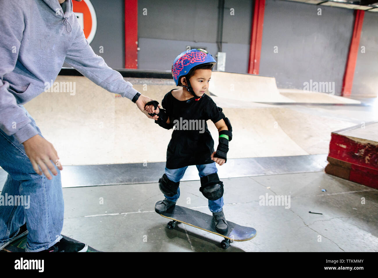 Skateboarding instructor holds onto hand of student as they skate Stock ...