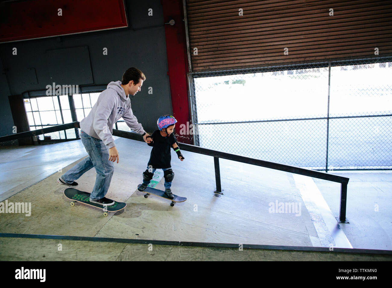 Skateboard instructor and young boy skate down a ramp holding hands ...
