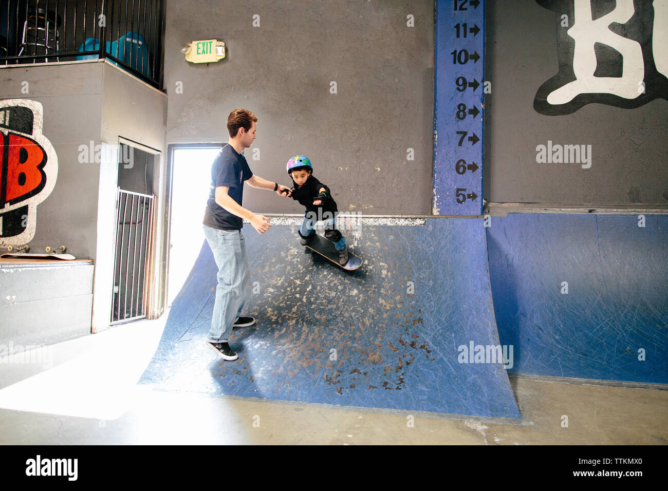 Skateboard instructor holds the hand of student while he is on ramp ...