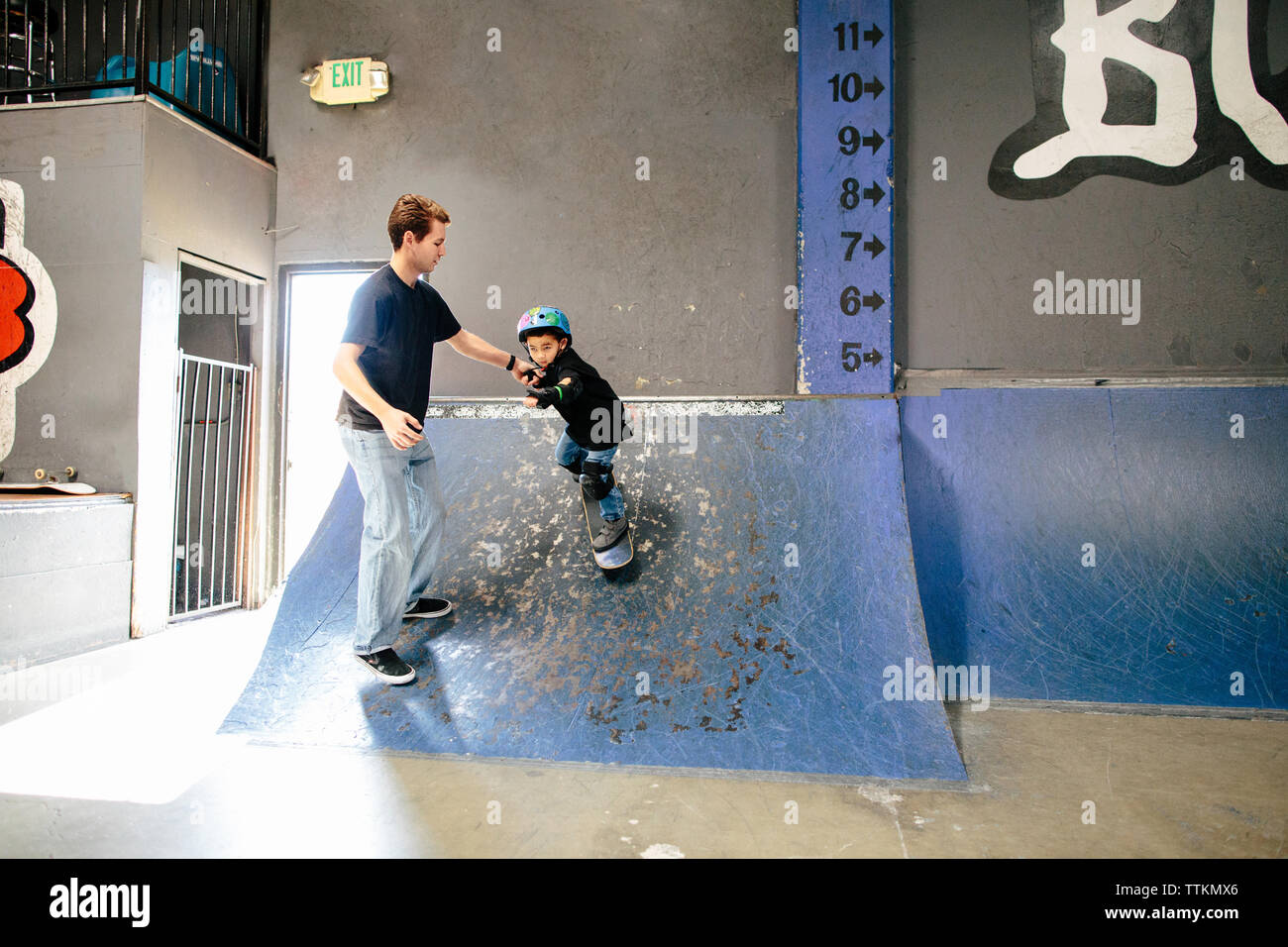 Skateboard instructor holds student's hand as he comes down a ramp ...