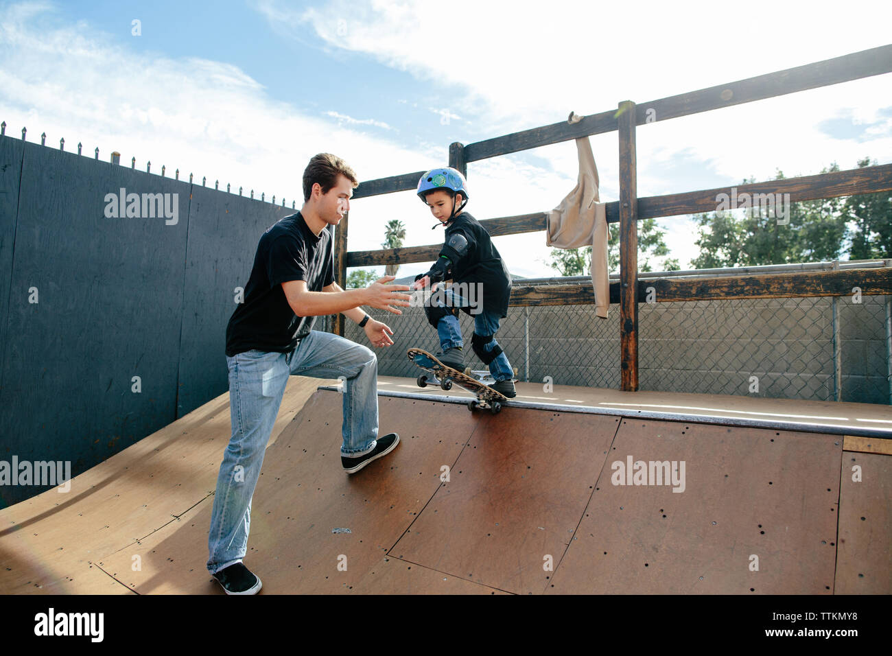 Young skater boy about to drop in on half pipe with instructor ready ...