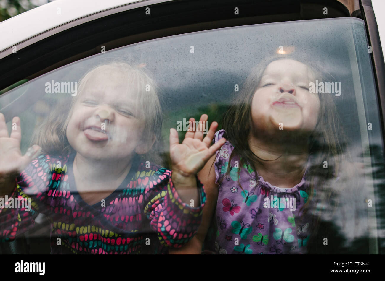 Playful sisters making faces while traveling in car seen through window ...